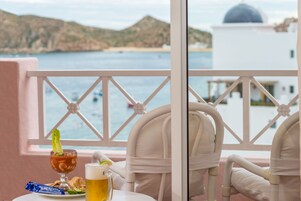 Varanda com mesa posta para dois, com vista para a costa, um edifício branco e uma cúpula azul.