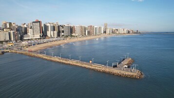 Paisagem costeira urbana com uma praia extensa, um cais de pedra e edifícios altos.