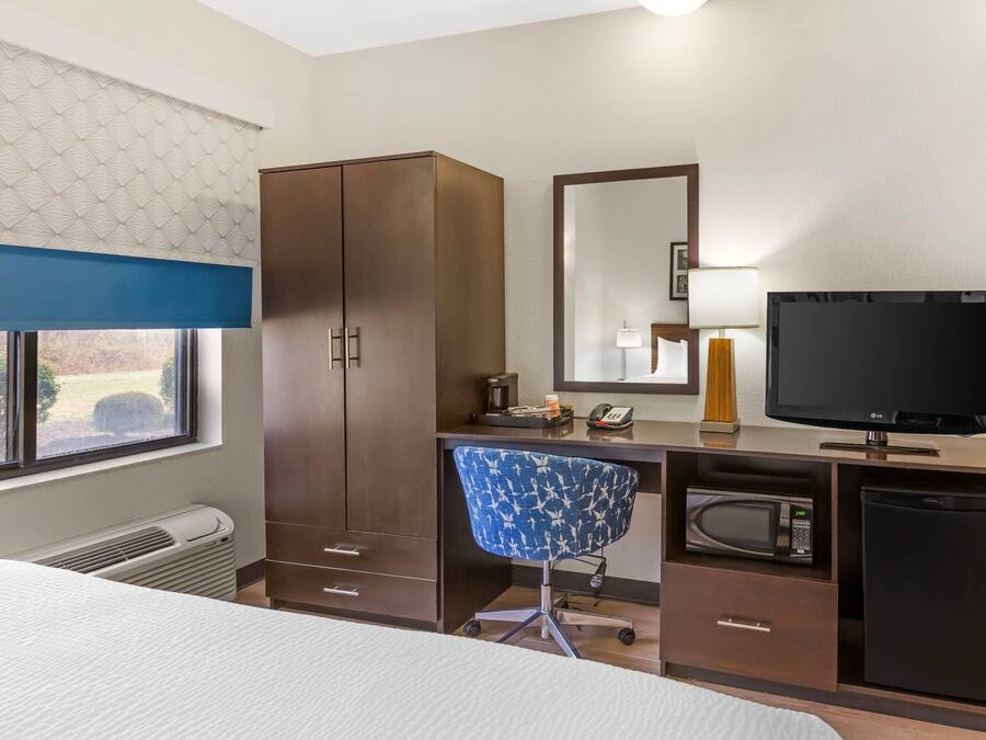 Quarto de hotel com cama, escrivaninha com computador, televisão, micro-ondas e frigorífico.