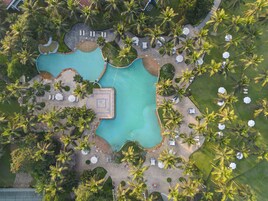 Vista aérea de um resort com piscina central, cercado por palmeiras e espreguiçadeiras.