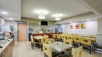 Um restaurante com várias mesas e cadeiras, uma área de cozinha e uma televisão na parede.