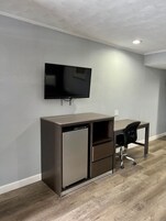 Quarto moderno com televisão integrada, pequeno espaço de cozinha e escrivaninha com cadeira.