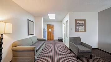 Quarto de hotel com carpete listrado, sofá, cadeira, abajur e porta para outro cômodo.
