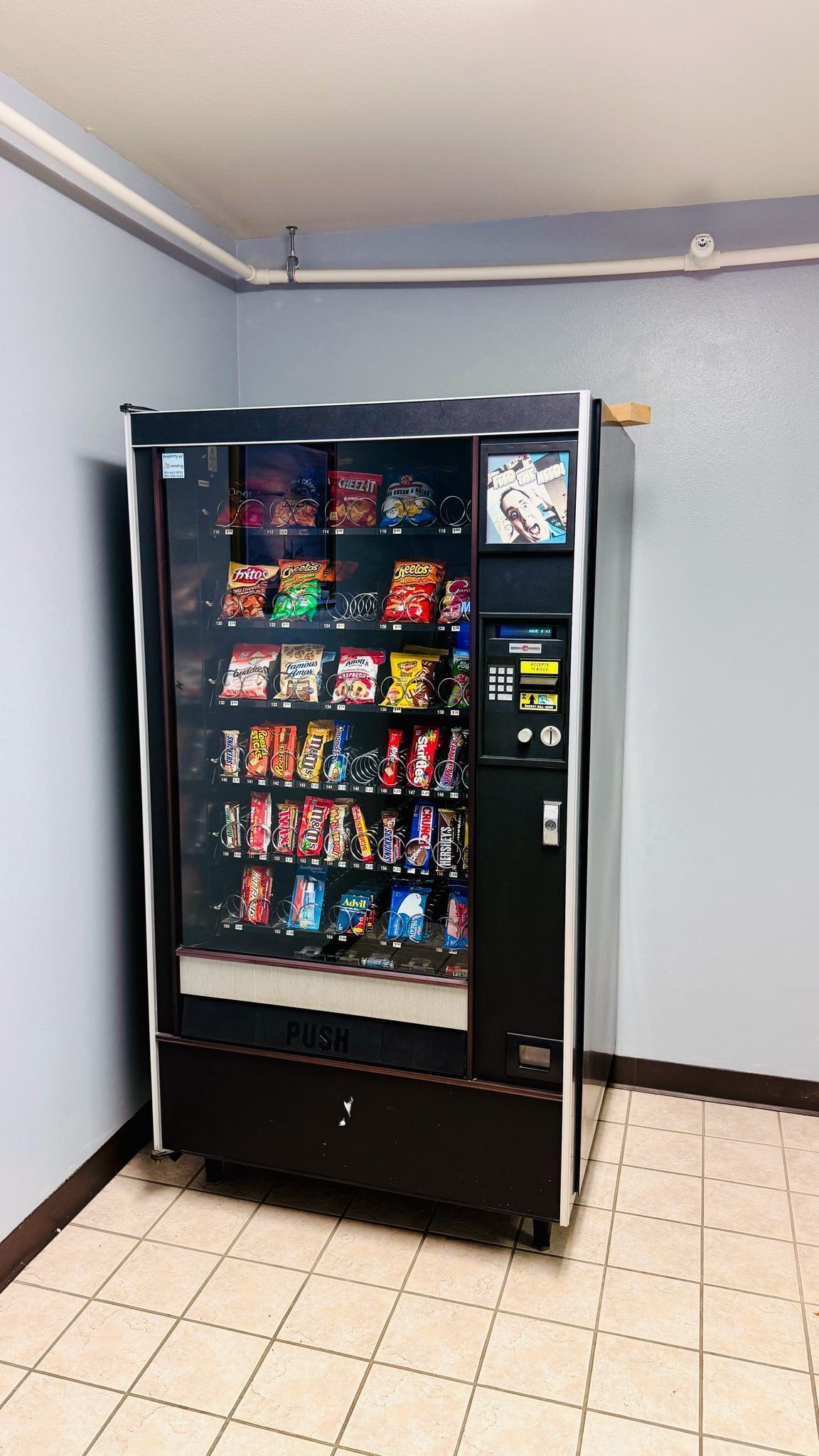 Máquina de vendas com diversos snacks e bebidas, situada num canto com chão em mosaico.
