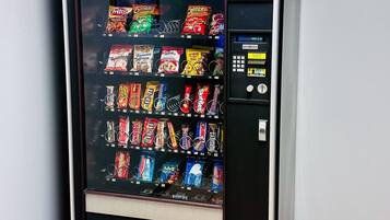 Máquina de vendas com diversos snacks e bebidas, situada num canto com chão em mosaico.