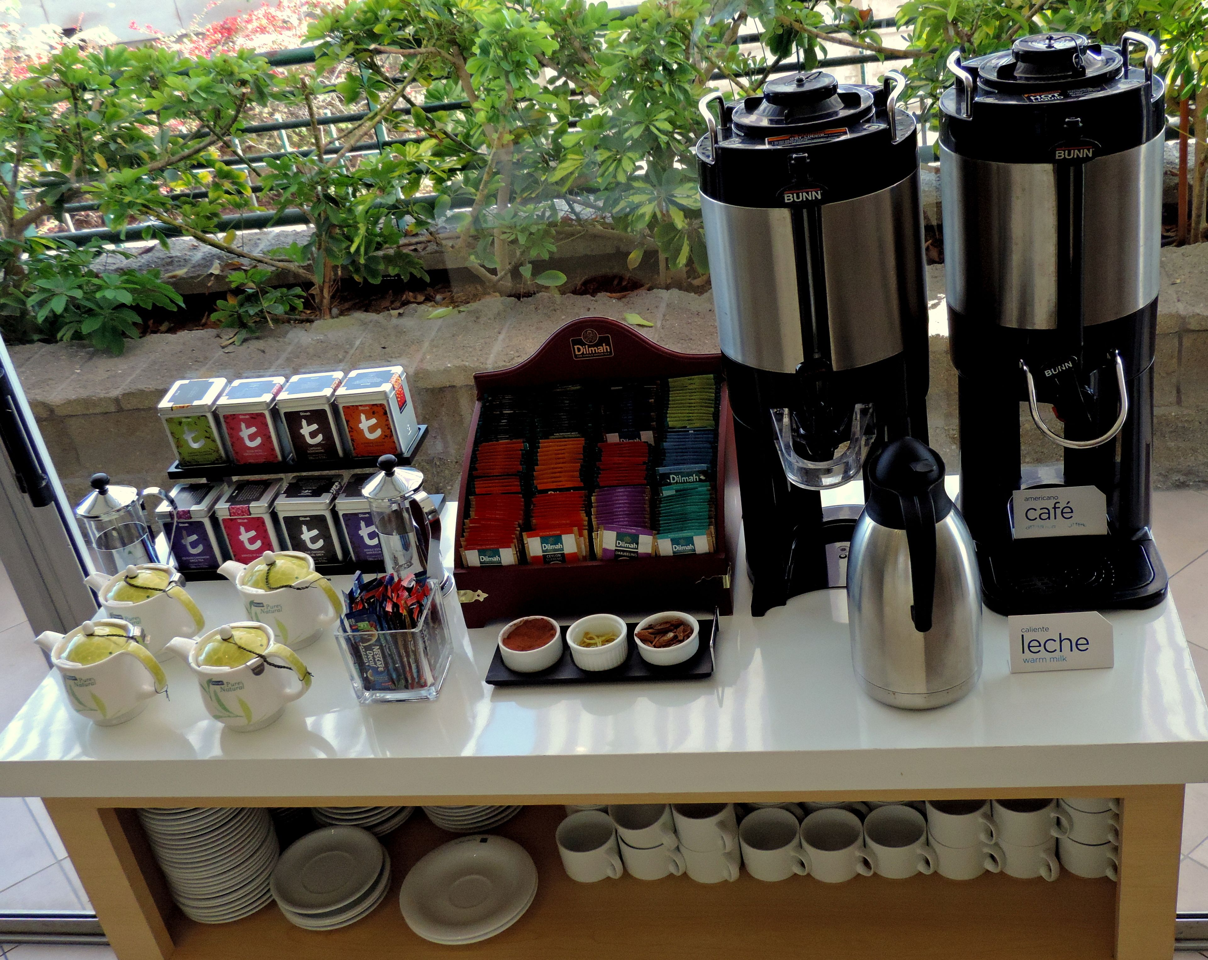 Estação de café com várias máquinas de café, uma variedade de cápsulas e uma seleção de xícaras e pires.