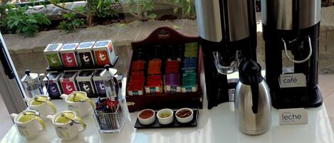 Estação de café com várias máquinas de café, uma variedade de cápsulas e uma seleção de xícaras e pires.