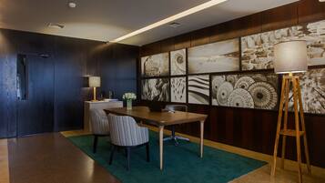 Um hall de hotel moderno com painel de madeira escura, uma mesa de madeira com duas cadeiras, um abajur e um tapete verde.