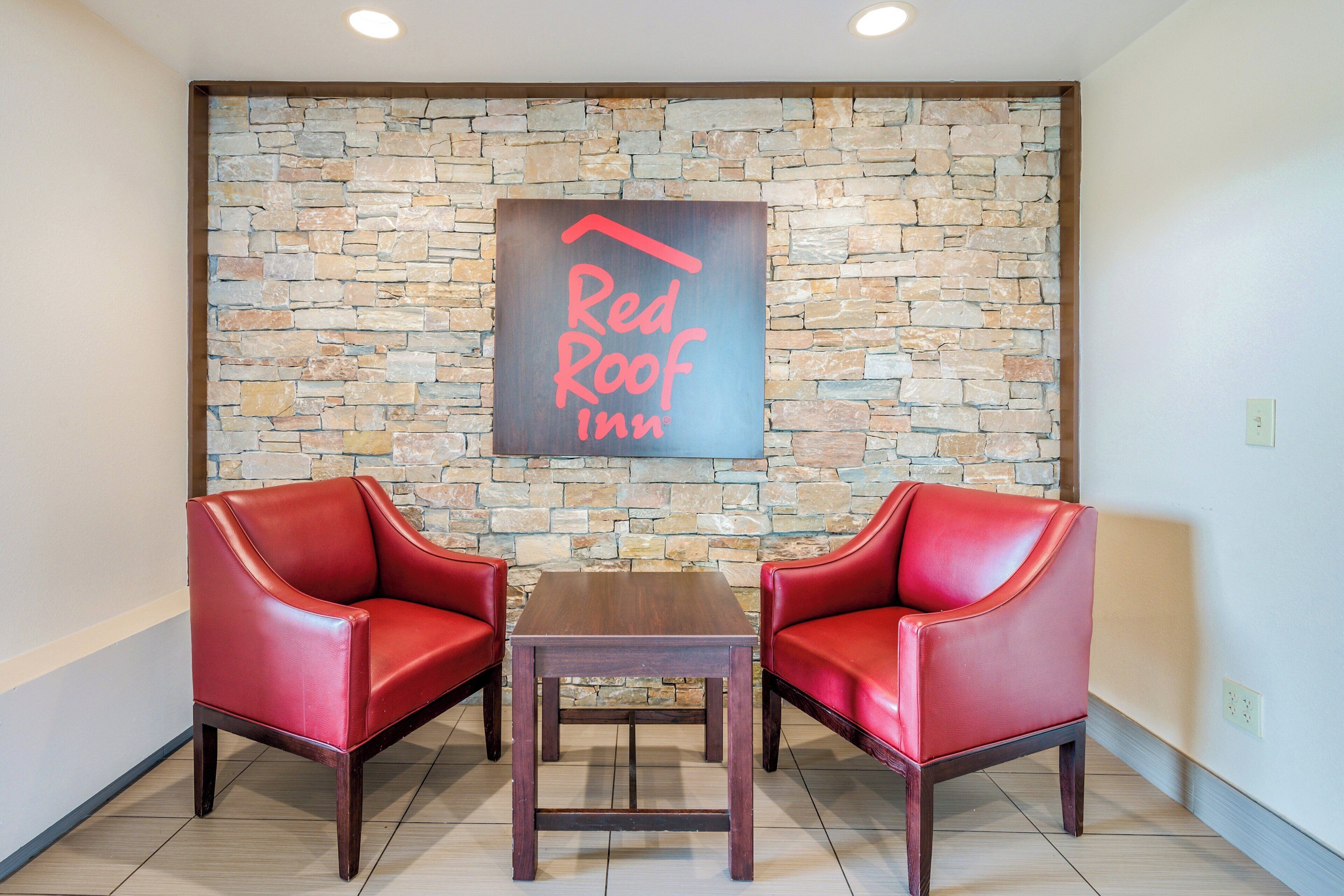 Lobby de um Red Roof Inn, com parede de pedra, duas poltronas de couro vermelho e uma mesa de madeira.