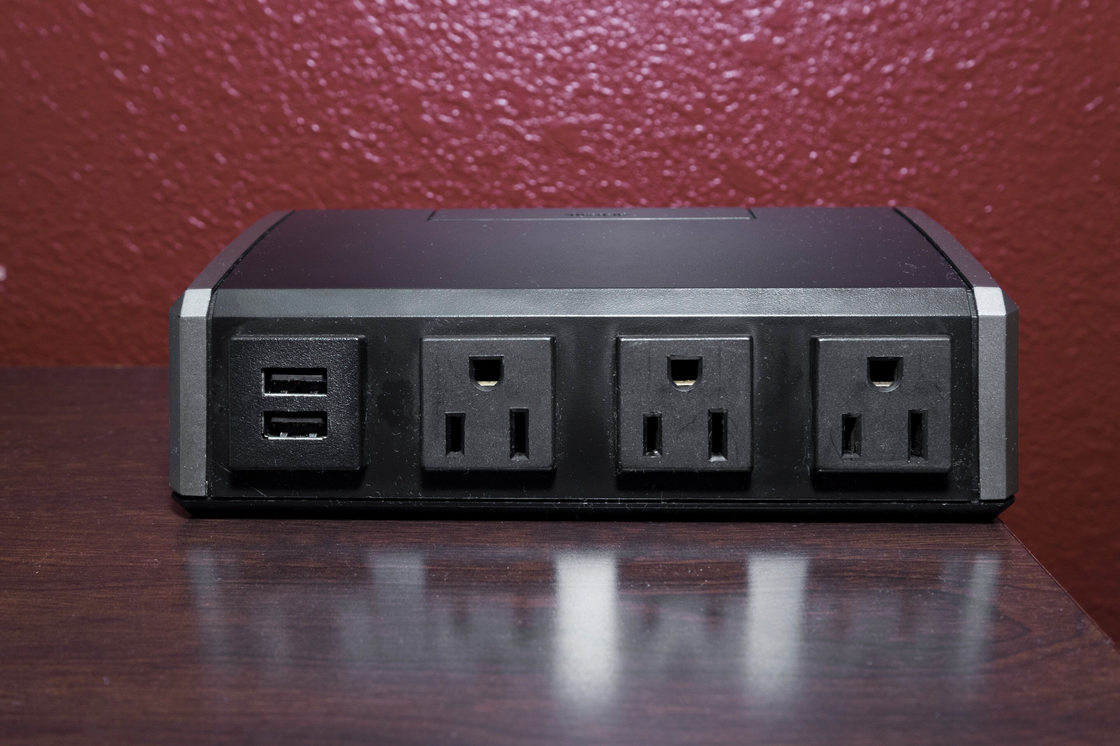 Uma régua de energia preta com quatro portas USB e duas tomadas elétricas sobre uma superfície de madeira.