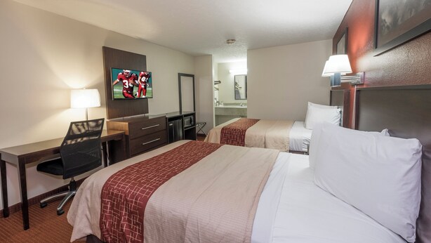 Quarto de hotel com duas camas, uma escrivaninha, uma cadeira, uma televisão e um espelho.