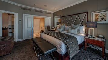 Quarto de hotel com cama grande, um banquinho, escrivaninha, cadeira, guarda-roupa e espelho.