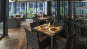 Restaurante moderno com mobiliário de vime, divisórias de vidro e vista para o exterior.