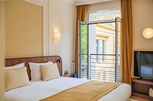 Quarto de hotel com cama, televisão, janela com cortinas e vista para o exterior.