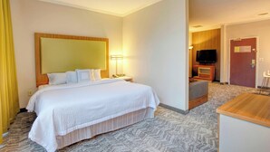 Quarto de hotel com uma cama grande, luminária de cabeceira, televisão e escrivaninha de madeira.