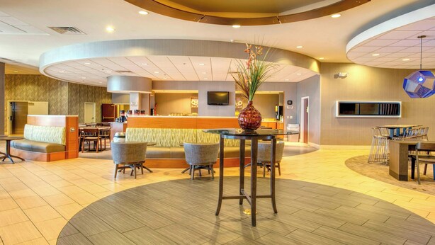 Um saguão de hotel com balcão de recepção, área de estar e uma televisão na parede.