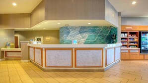 Uma área de recepção de hotel, com um balcão, um mural com um mapa verde e um refrigerador cheio de bebidas.