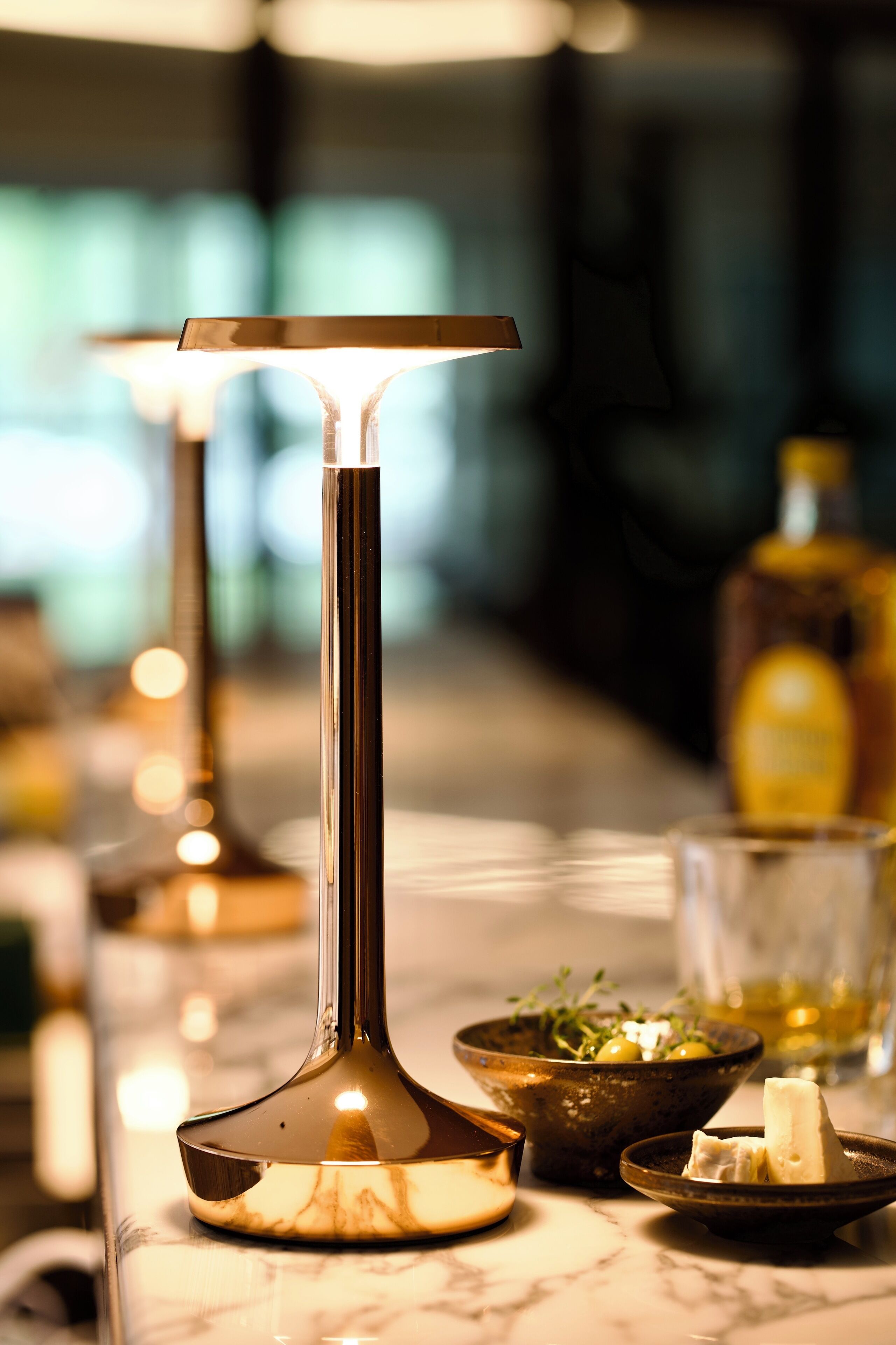 Um bar com iluminação moderna, uma tigela de azeitonas, um copo de azeite e um pequeno prato de queijo.