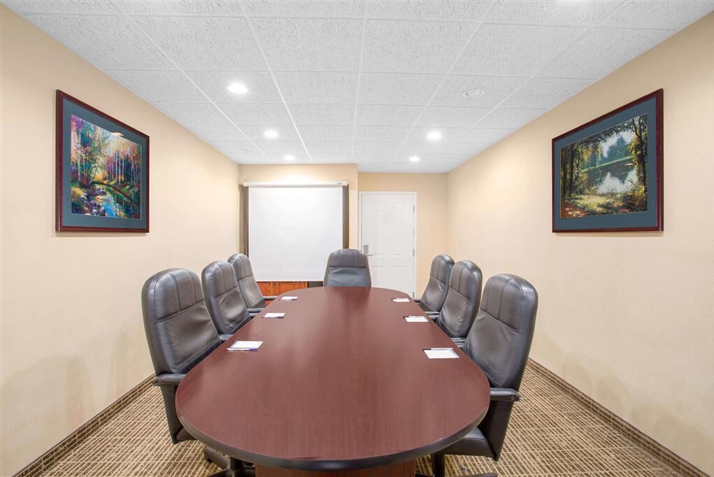 Uma sala de conferências com uma grande mesa oval, cadeiras de couro e duas pinturas emolduradas de paisagens nas paredes.
