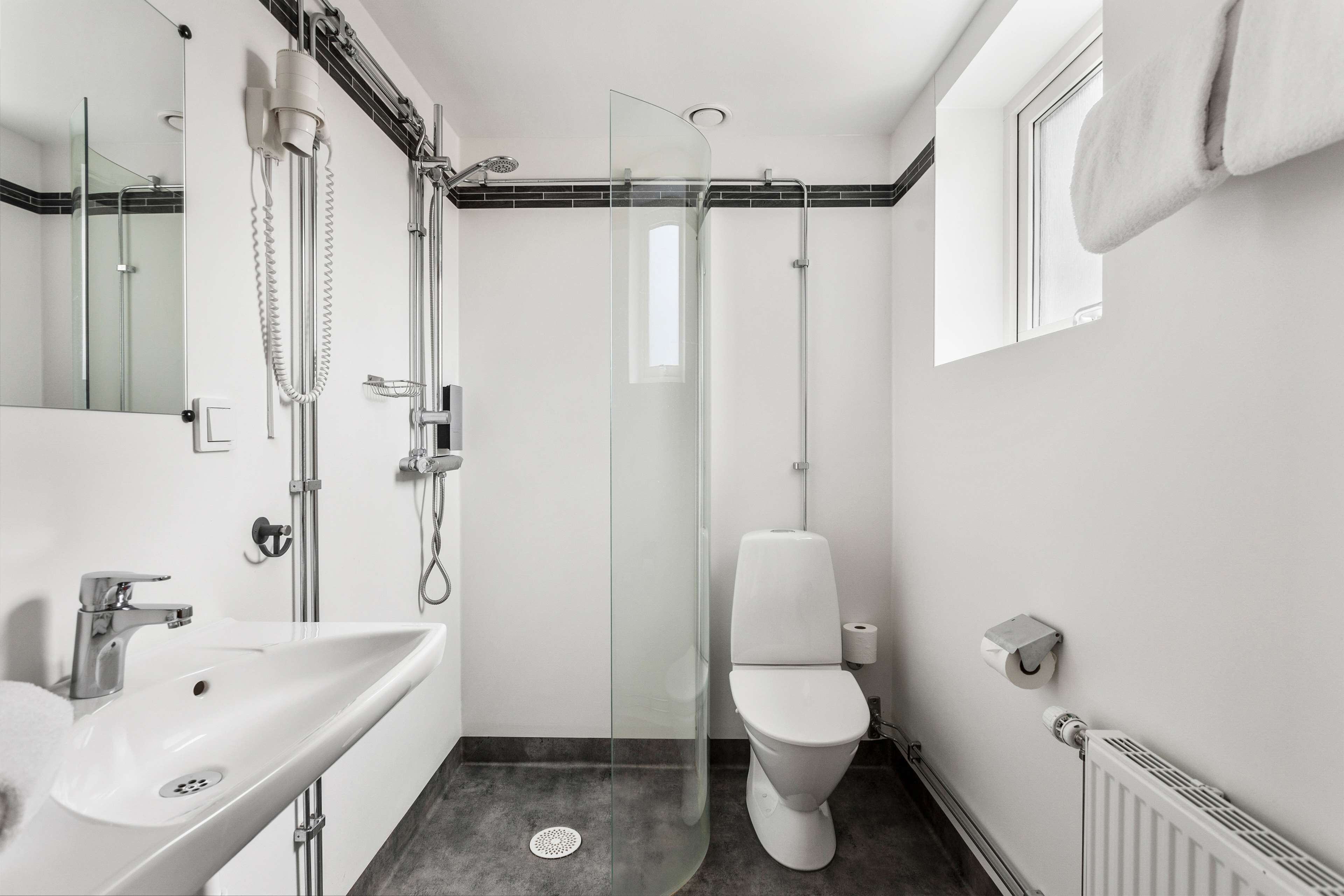 Uma casa de banho moderna com chuveiro envolto em vidro, lavatório branco e sanita.