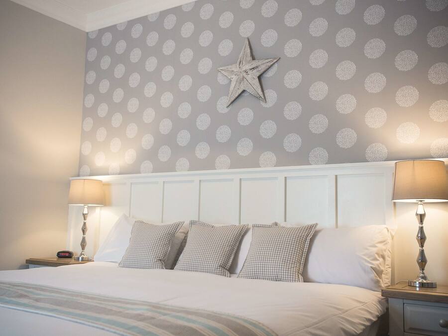 Uma cama bem arrumada com almofadas xadrez, uma decoração de estrela na parede e duas luminárias de cabeceira.
