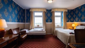 Quarto de hotel com duas camas, uma escrivaninha, uma cadeira e uma janela com cortinas.