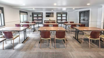 Sala de conferência com várias mesas e cadeiras, piso coberto de carpete e grandes janelas.