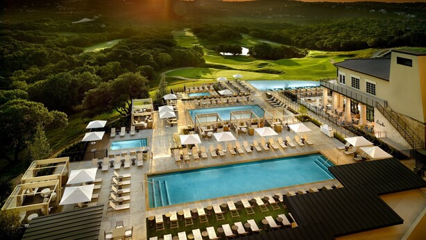 Um resort com várias piscinas, espreguiçadeiras e um campo de golfe ao fundo.