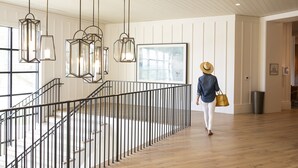 Um espaço amplo com escada de madeira, luminárias pendentes em estilo lanterna e um grande quadro abstrato na parede.