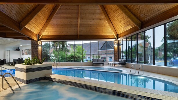 Piscina interior moderna com teto de madeira e grandes janelas que oferecem vista da região circundante.