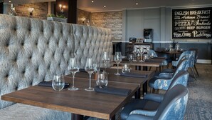 Um restaurante com área de estar com cabeceira estofada, mesas de madeira e cadeiras estofadas em azul.