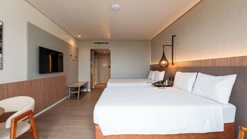 Quarto de hotel com duas camas, uma mesa, uma cadeira, uma televisão e um abajur.