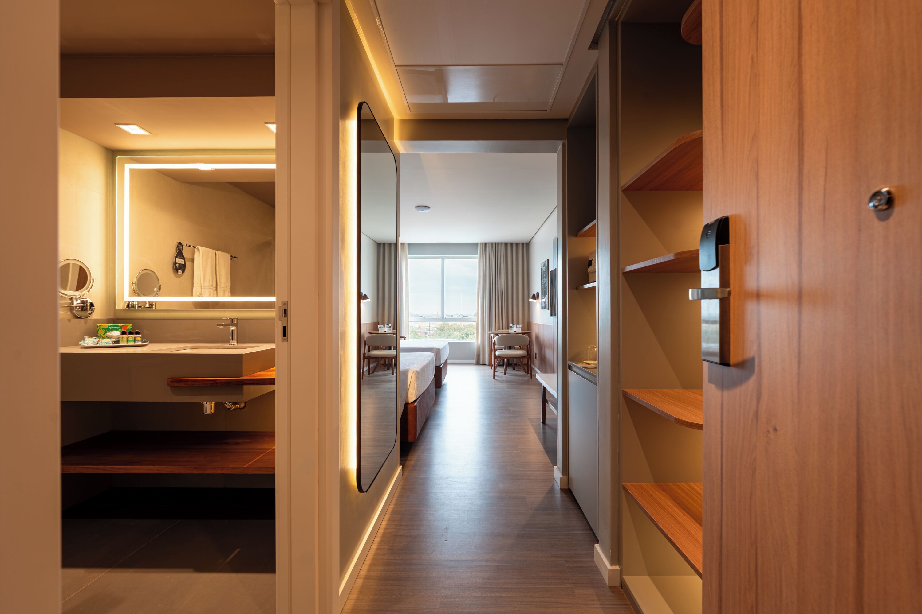 Quarto de hotel com banheiro, corredor e cama.
