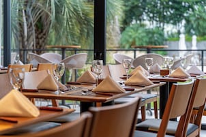 Um restaurante com mesas preparadas para refeições, cadeiras e vista para o verde lá fora.