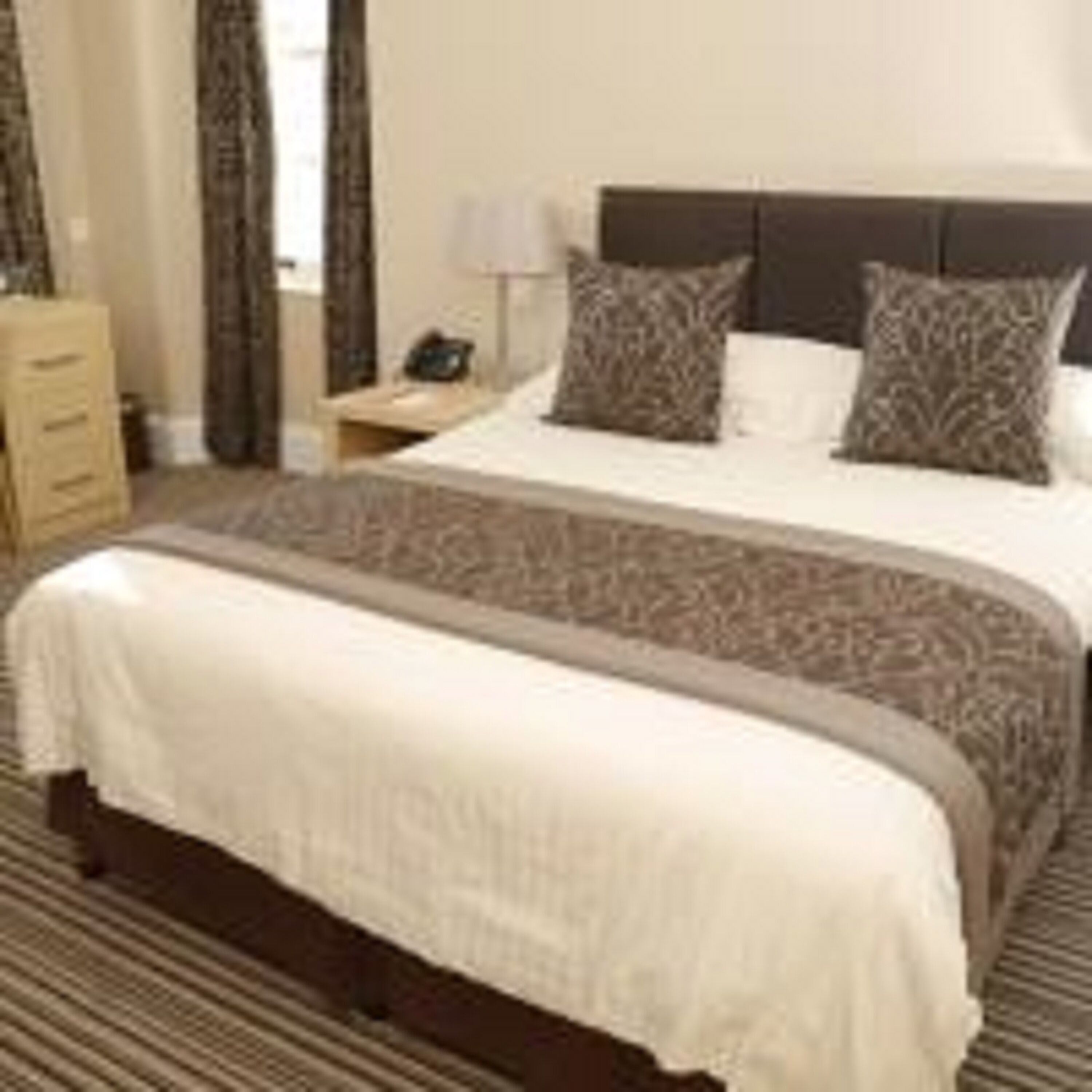 Quarto de hotel com uma cama grande, mesa de cabeceira, abajur e cômoda.