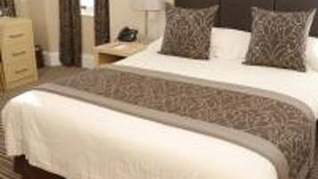 Quarto de hotel com uma cama grande, mesa de cabeceira, abajur e cômoda.