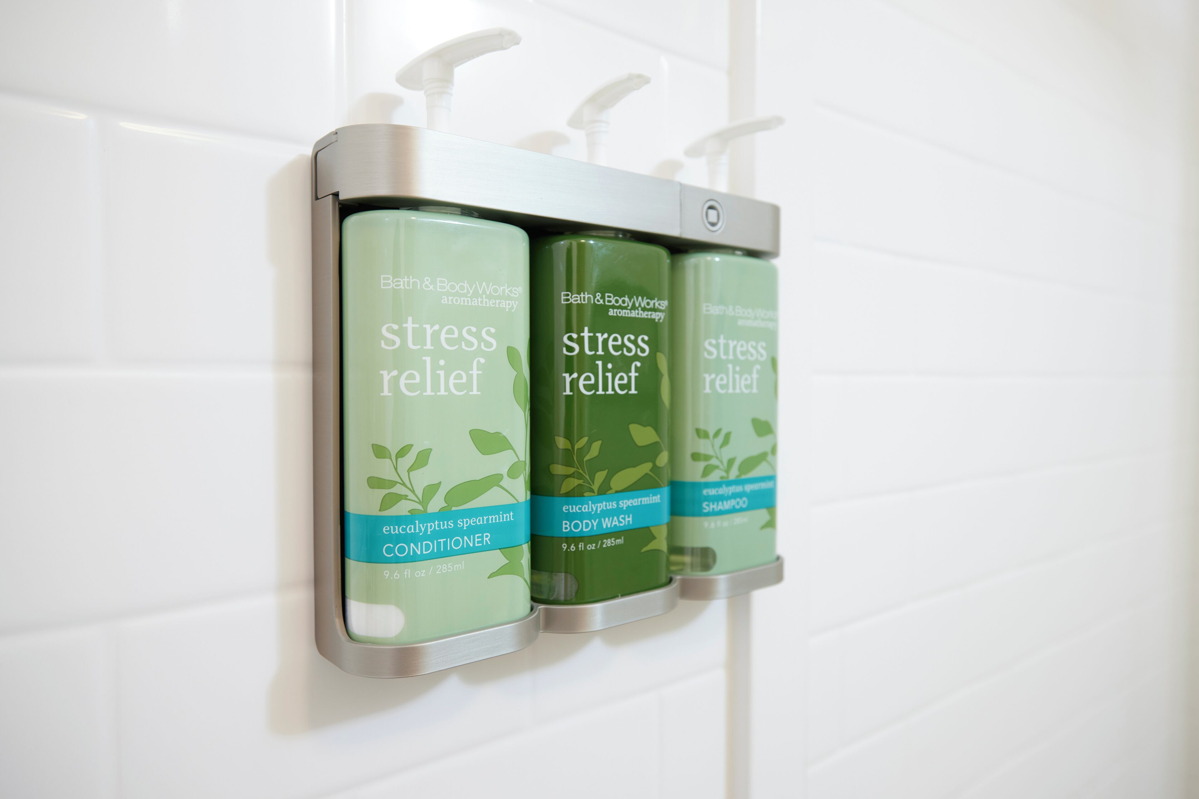 Um dispensador fixado na parede com três frascos de produtos de aromaterapia Bath & Body Works rotulados 'alívio do stress'.
