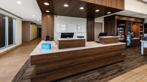 Bancada de recepção de hotel com balcão de madeira, tela digital e minibar.