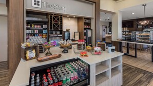 Uma loja de hotel com seções de produtos refrigerados e congelados, diversos snacks e uma variedade de garrafas de água.