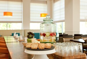 Uma área de refeições com uma mesa comprida, um pote de vidro com fatias de fruta e vários bastões de granola em um prato.