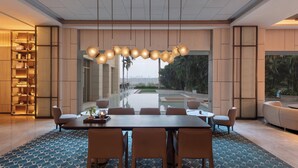 Uma área de refeições moderna com uma mesa comprida e cadeiras, um tapete estampado e uma grande janela com vista para um jardim.