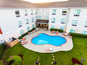 Pátio de hotel com piscina, espreguiçadeiras e área de estar coberta.