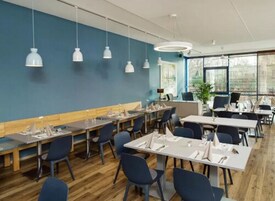 Uma sala de jantar moderna com mesas de madeira e cadeiras azuis, com iluminação pendente e janelas amplas.