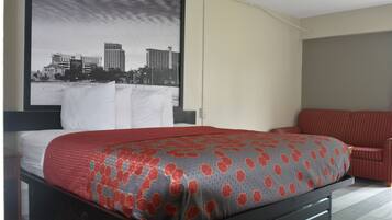 Um quarto moderno com uma cama, um edredom vermelho e cinza com padrão, uma janela grande com vista para a cidade e uma poltrona estofada em vermelho.