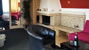 Uma sala de estar com lareira de tijolos, um sofá de couro, um sofá vermelho e uma mesa de jantar com uma garrafa e um copo.