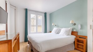 Quarto de hotel com cama, mesas de cabeceira de madeira, escrivaninha e televisão.