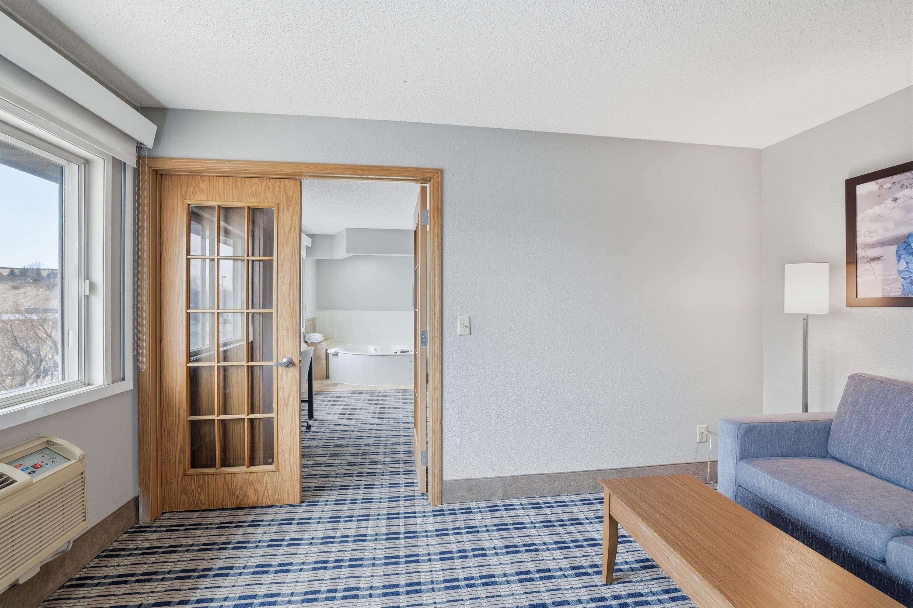 Um quarto com porta de madeira, chão quadriculado em azul e branco, sofá azul, mesa de centro de madeira e um quadro na parede.