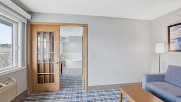 Um quarto com porta de madeira, chão quadriculado em azul e branco, sofá azul, mesa de centro de madeira e um quadro na parede.
