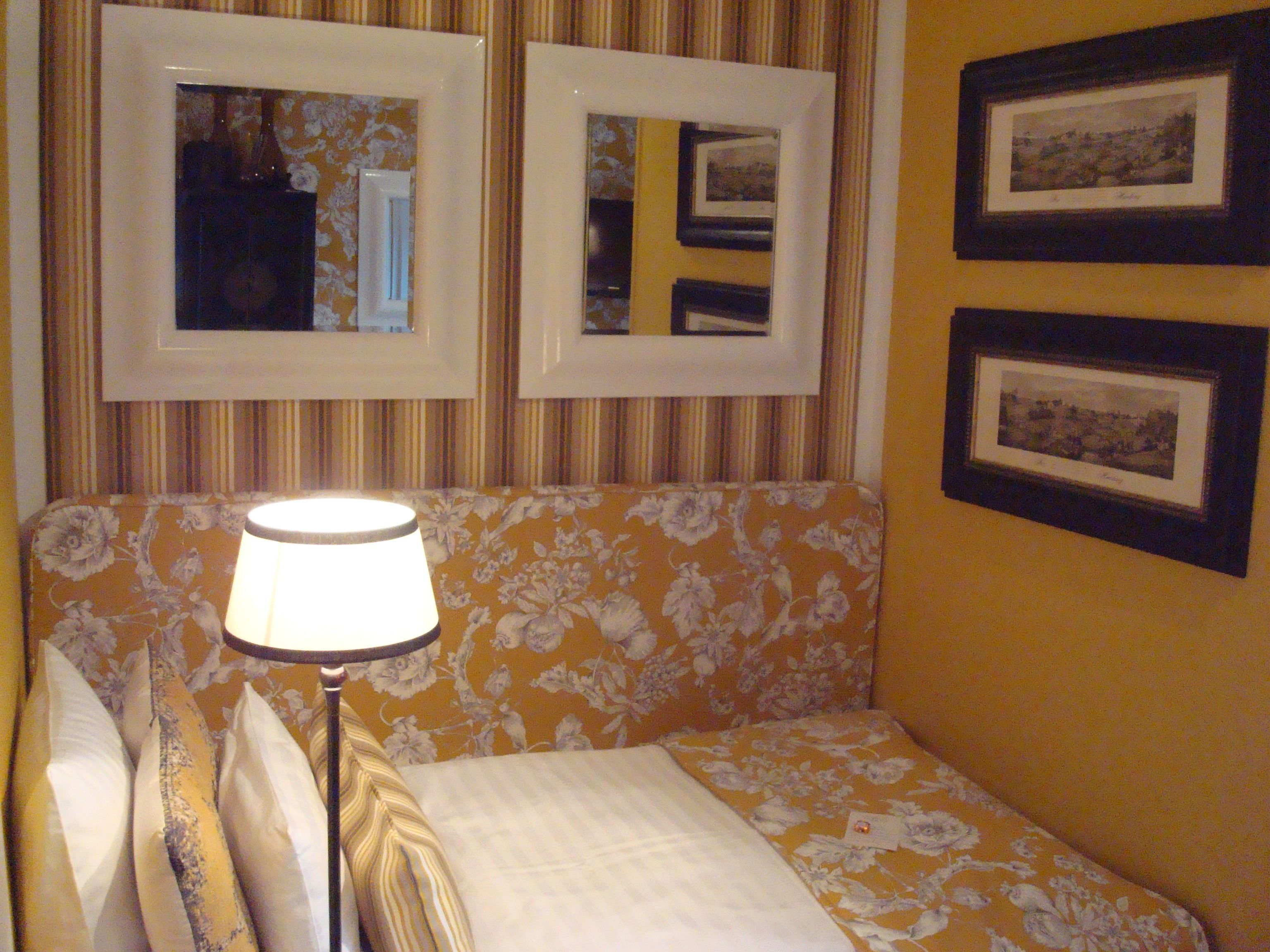 Quarto com sofá floral, uma luminária e três quadros na parede.