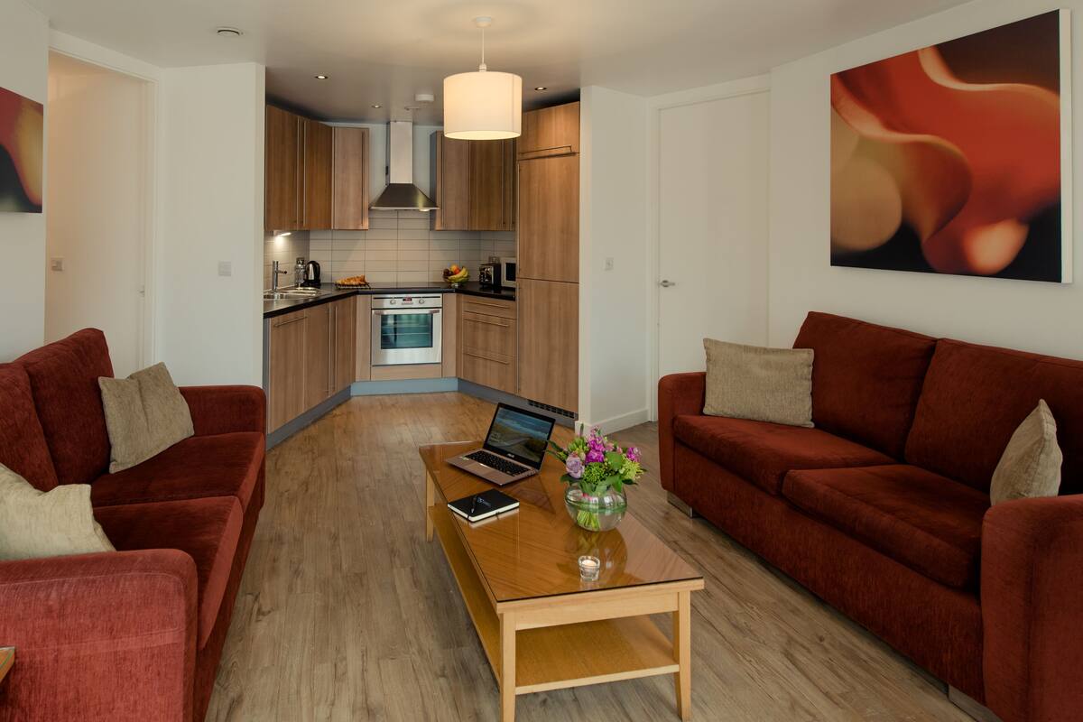 Uma sala de estar moderna com uma mesa de centro de madeira, sofás vermelhos e um laptop.